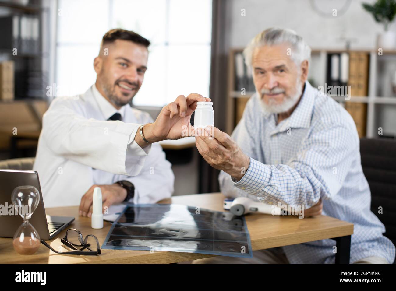Portrait of happy aged patient and qualified doctor sitting at desk and ...