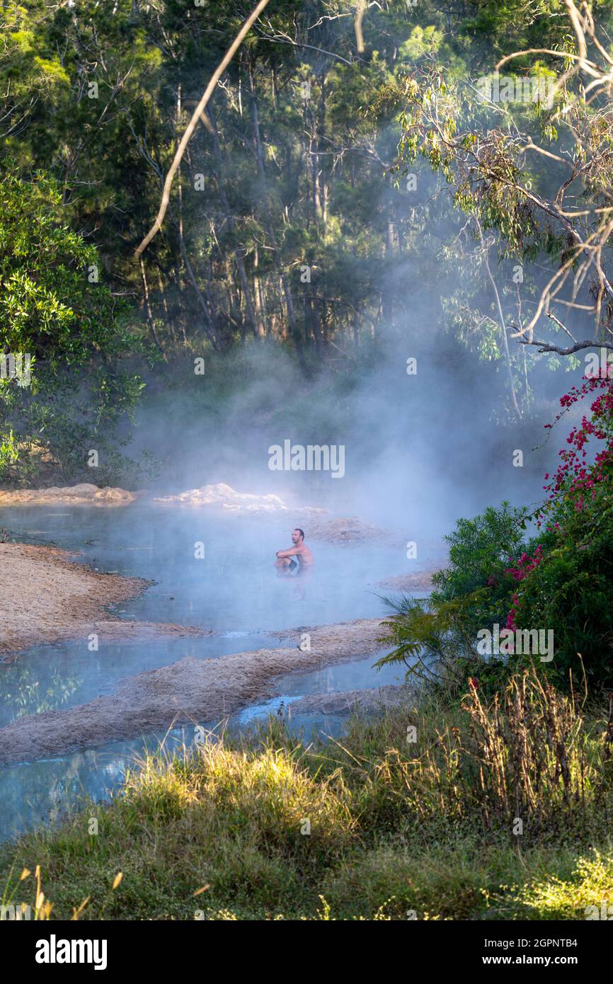 Mist rising in the early morning as man sits in shallow hot water pool ...