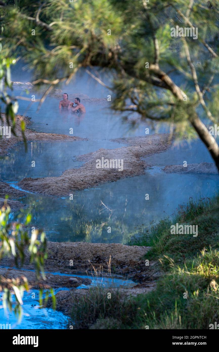 Mist rising in the early morning as man sits in shallow hot water pool ...