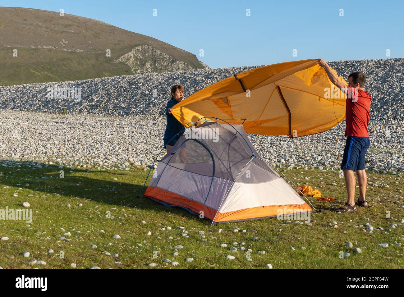 Young Caucasian tourists setting up a tent at a campsite surrounded by ...