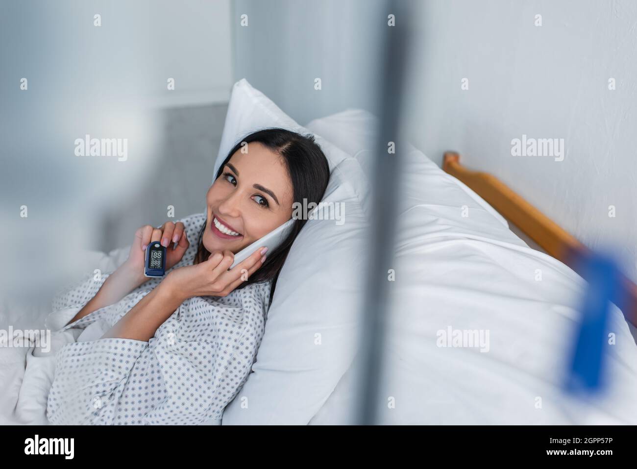 positive woman with oximeter on finger talking on smartphone while ...