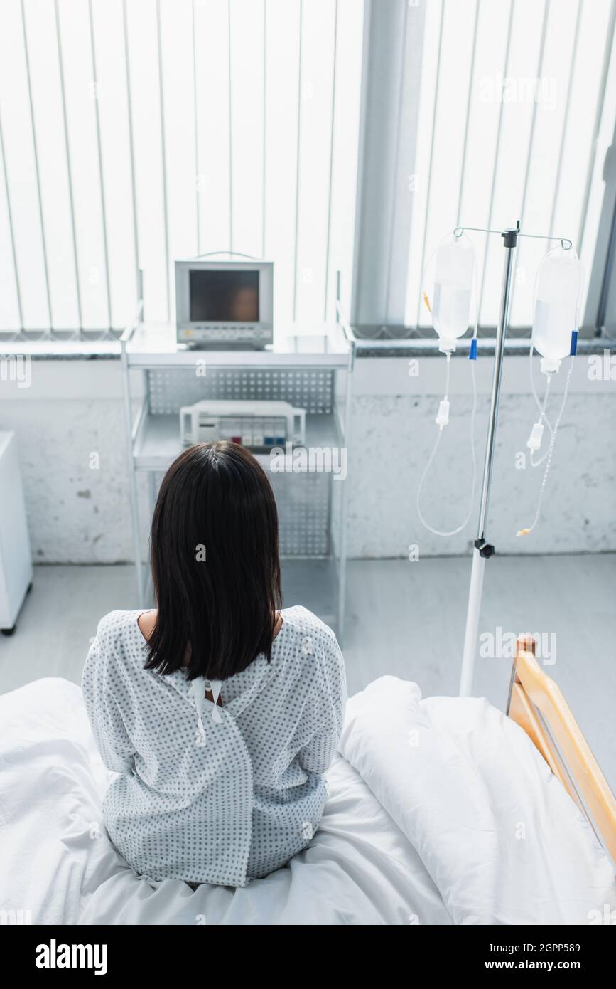 back view of woman in patient gown sitting on hospital bed Stock Photo ...