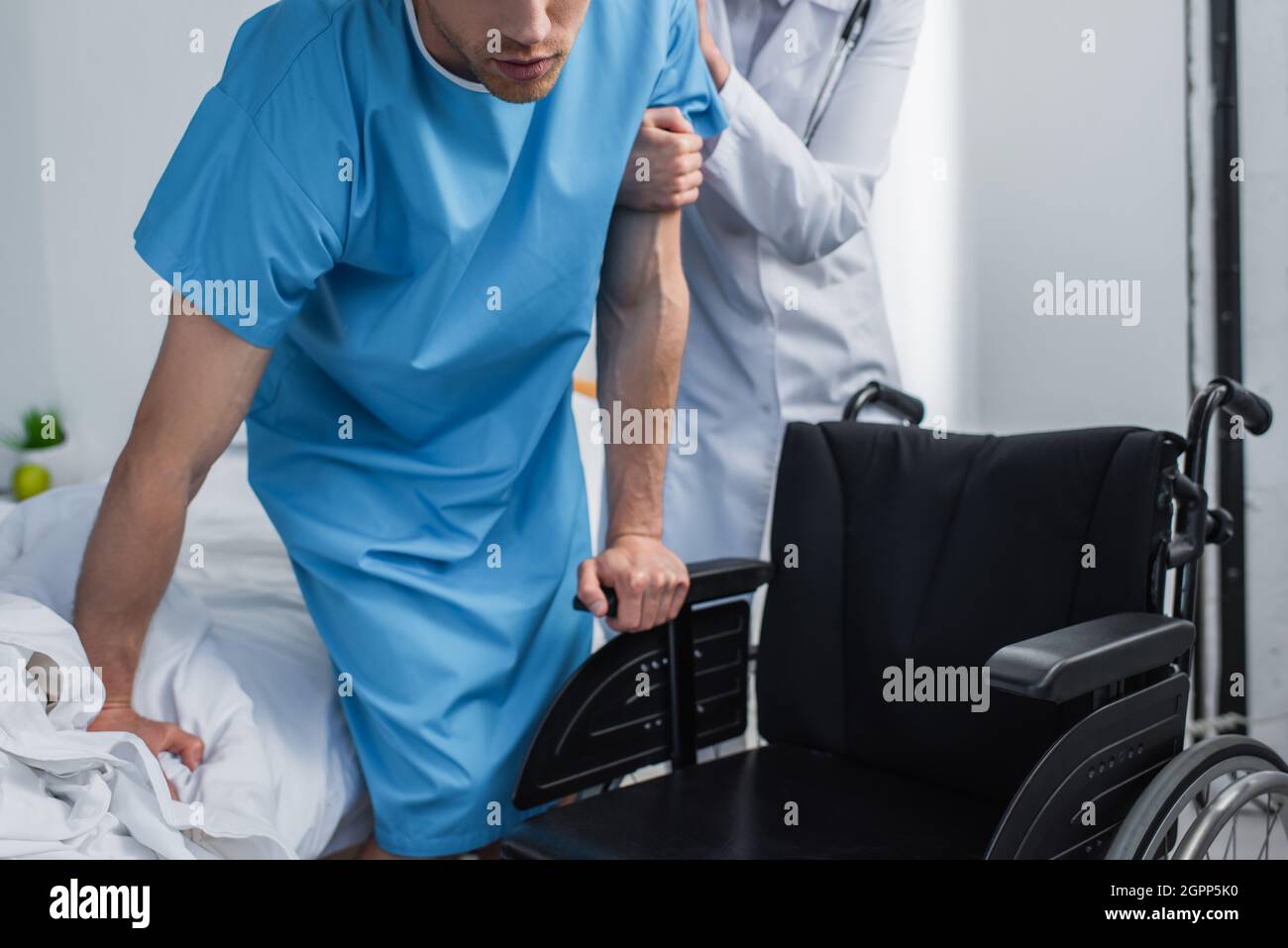 cropped view of doctor in white coat helping patient get up from ...
