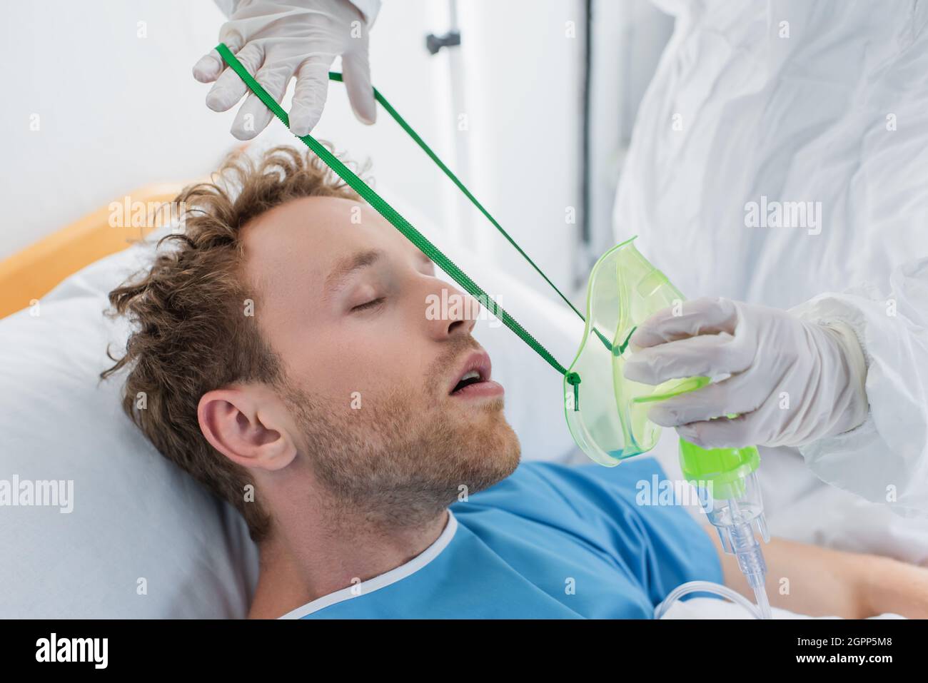 doctor in hazmat suit and latex gloves placing oxygen mask on sick ...