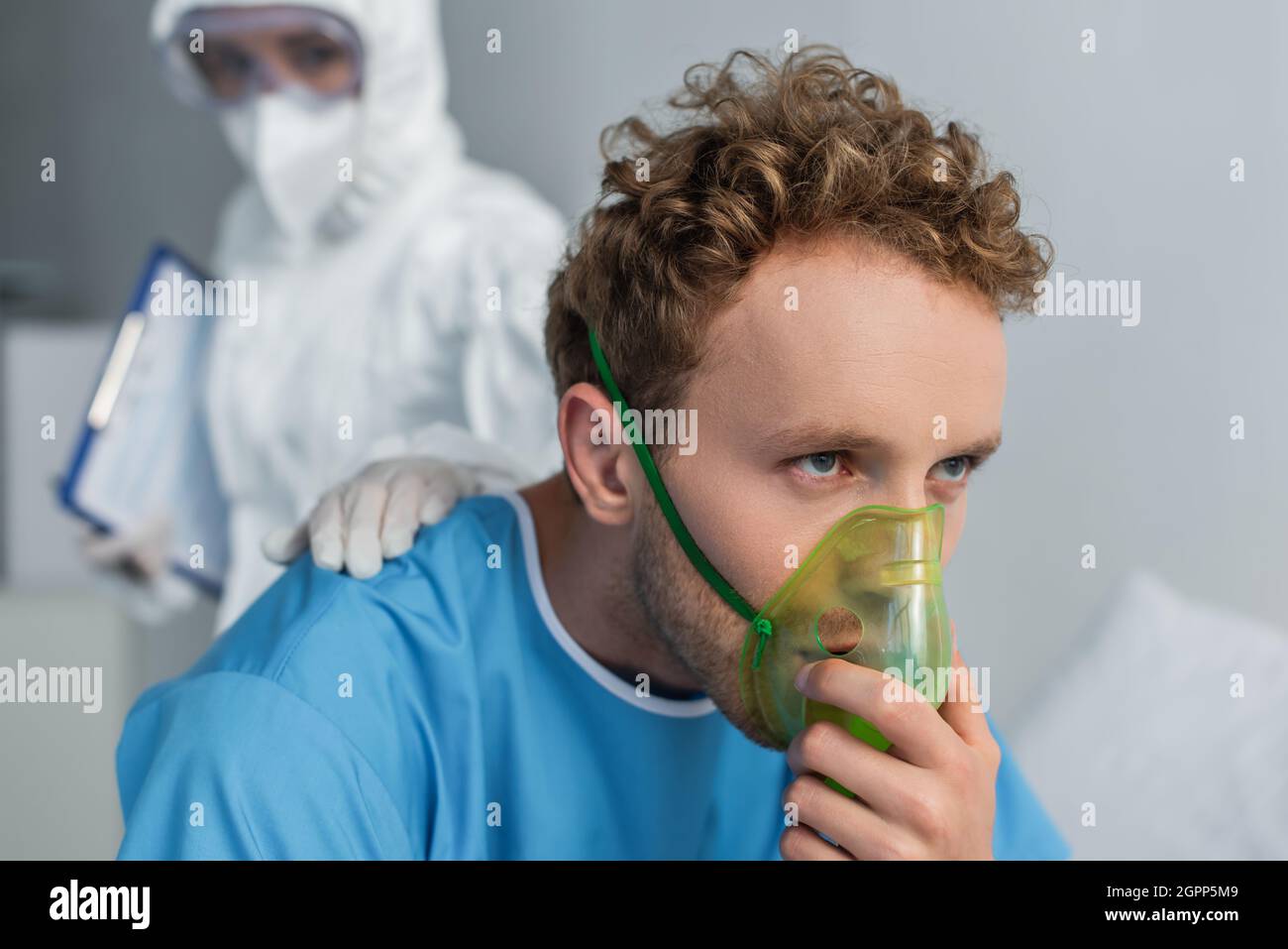 blurred doctor in hazmat suit calming sick patient breathing in oxygen ...
