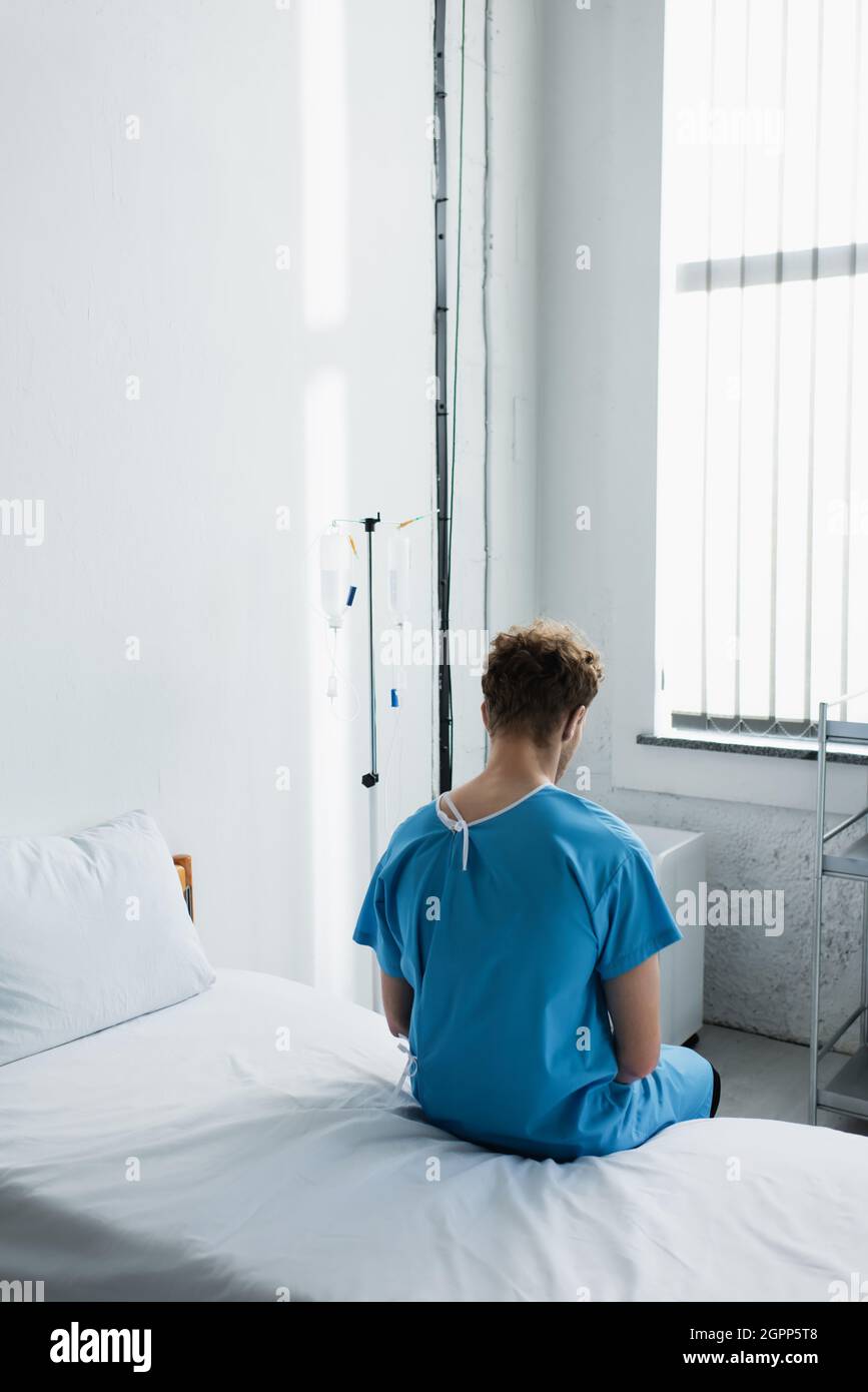 back view of curly man in patient gown sitting on hospital bed Stock ...
