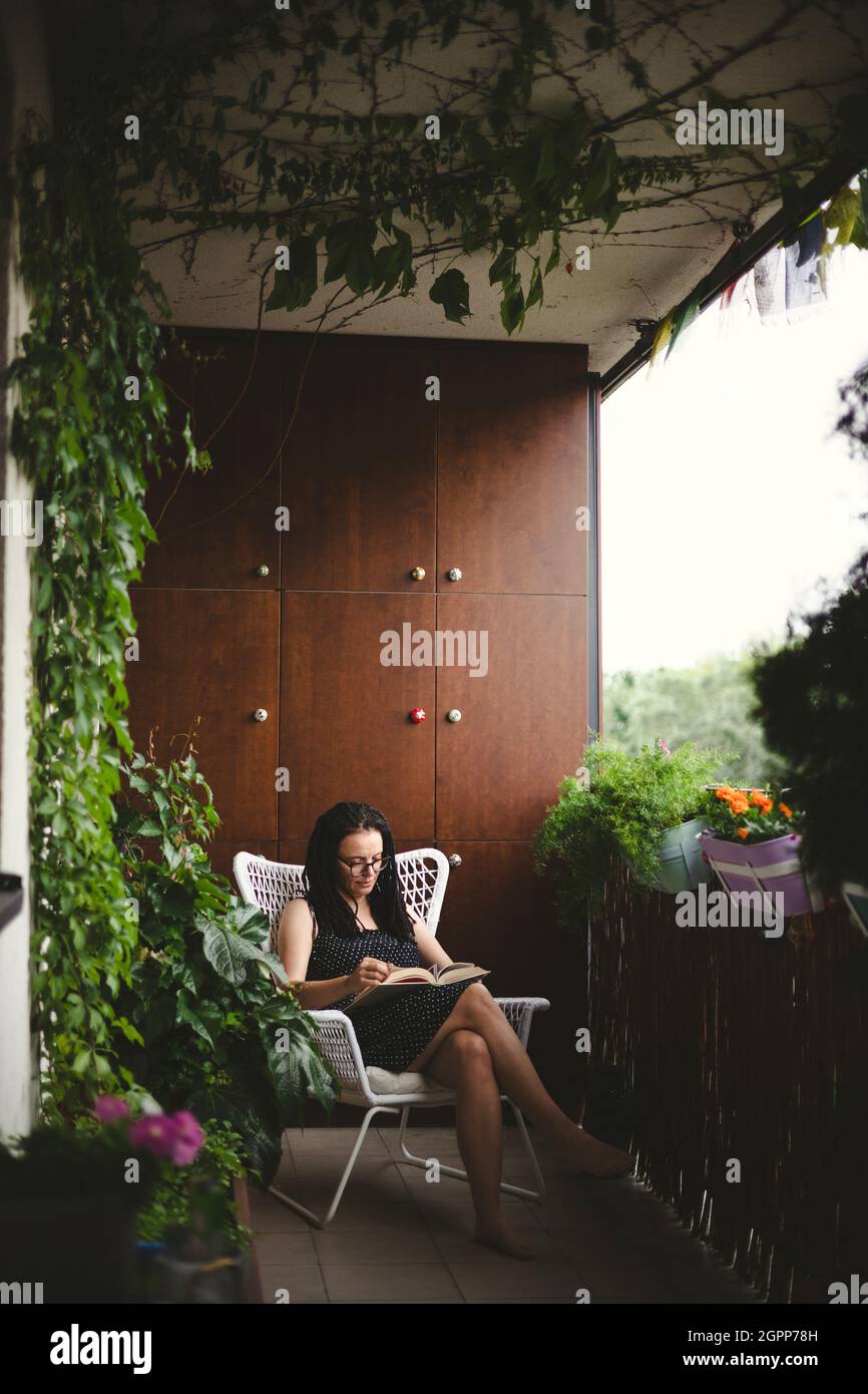 Woman reading a book on a green balcony Stock Photo - Alamy