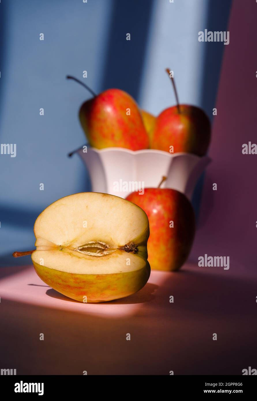 Up view of apples in a container, a sliced apple on the table on a pink ...