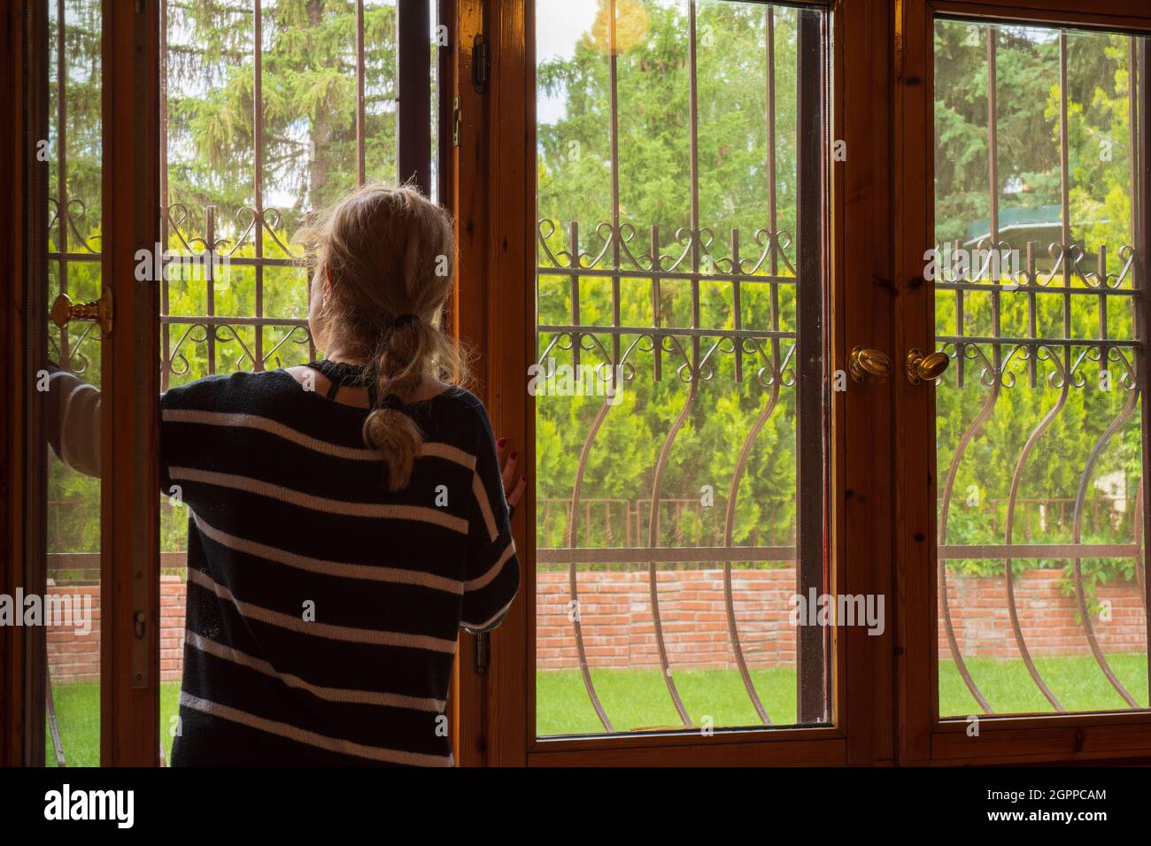 The young woman watches the garden of her house through the barred ...