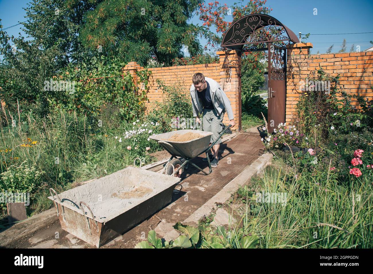 A man unloads sand into a cement mixture for pouring a garden path ...