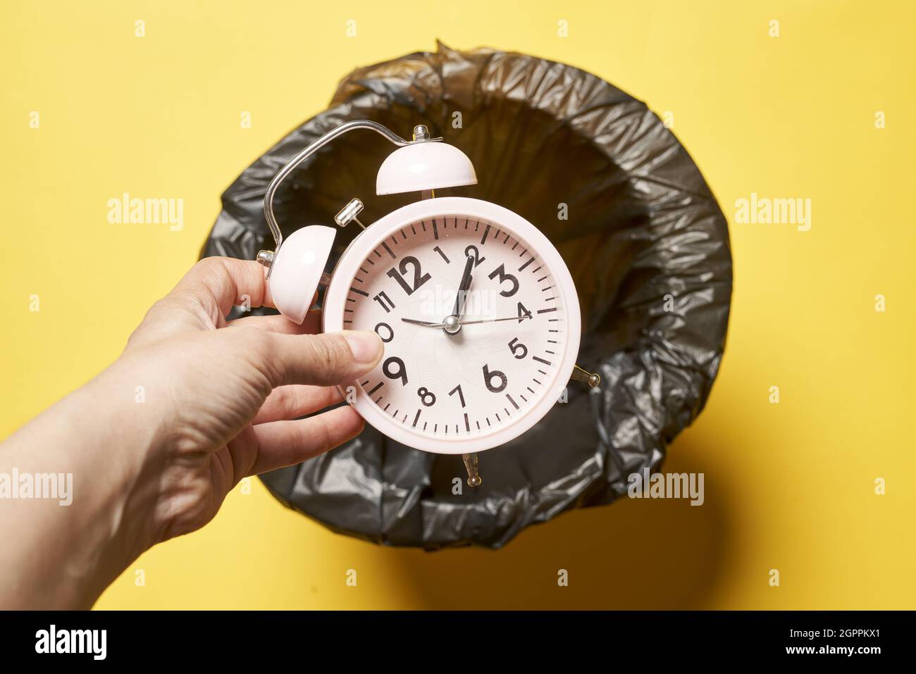 Top view of a hand throwing an alarm clock into a trash bin on yellow ...