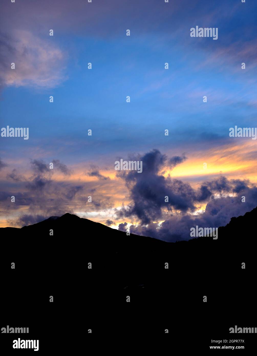 Dark brooding clouds and a vividly coloured sky over a mountain in ...