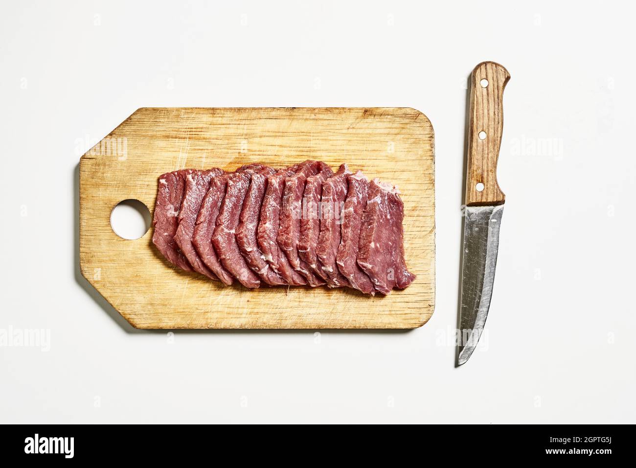 Overhead shot of sliced raw meat on wooden board with knife isolated on ...