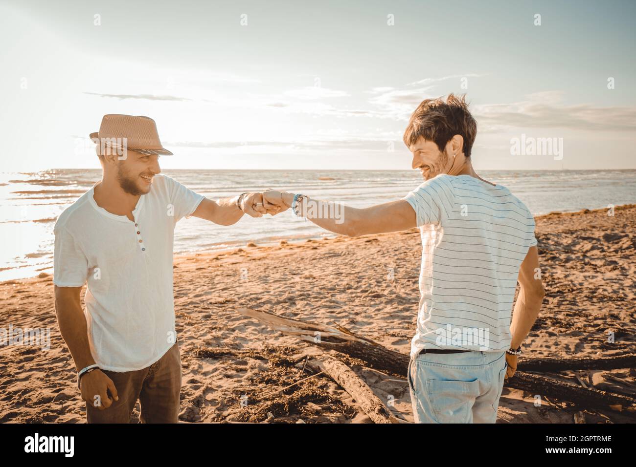 Two caucasian smiling guys on the beach greeting each other with touch ...