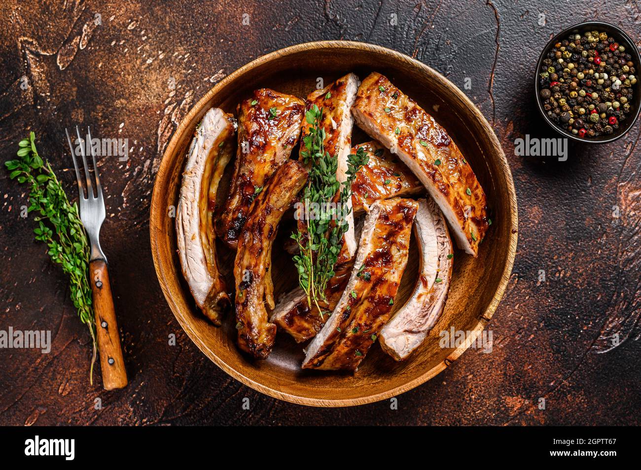 Cut BBQ grilled pork rack spareribs in a wooden plate. Dark background ...