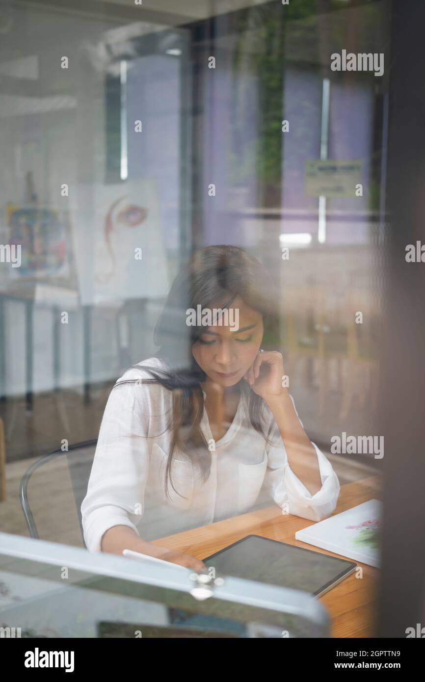View through glass window creative designer woman working in her art ...