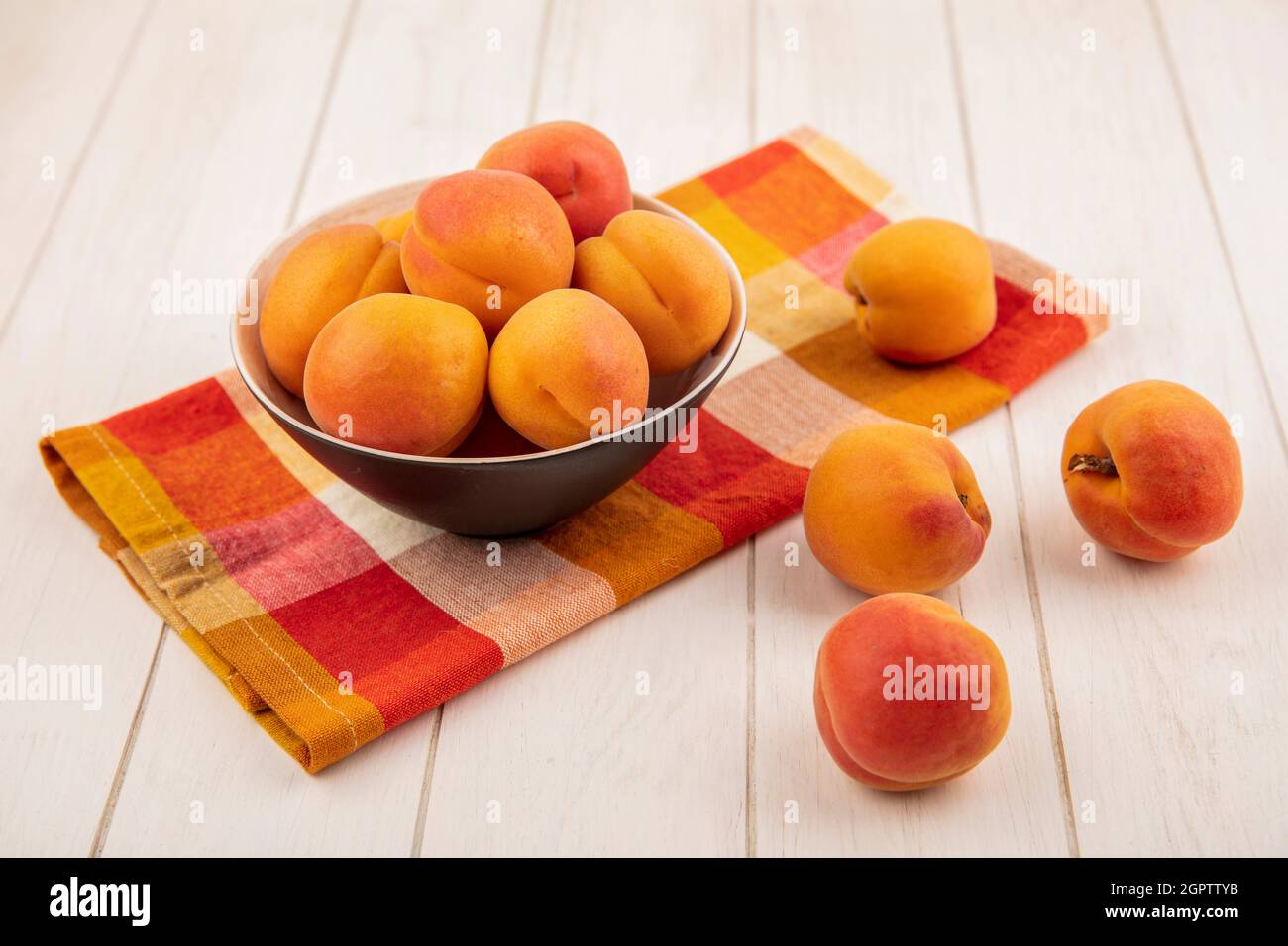 side view of peaches in bowl on plaid cloth and on wooden background ...