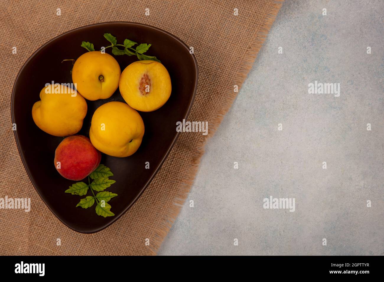 top view fresh juicy yellow peaches on a bowl on a sack cloth on a ...