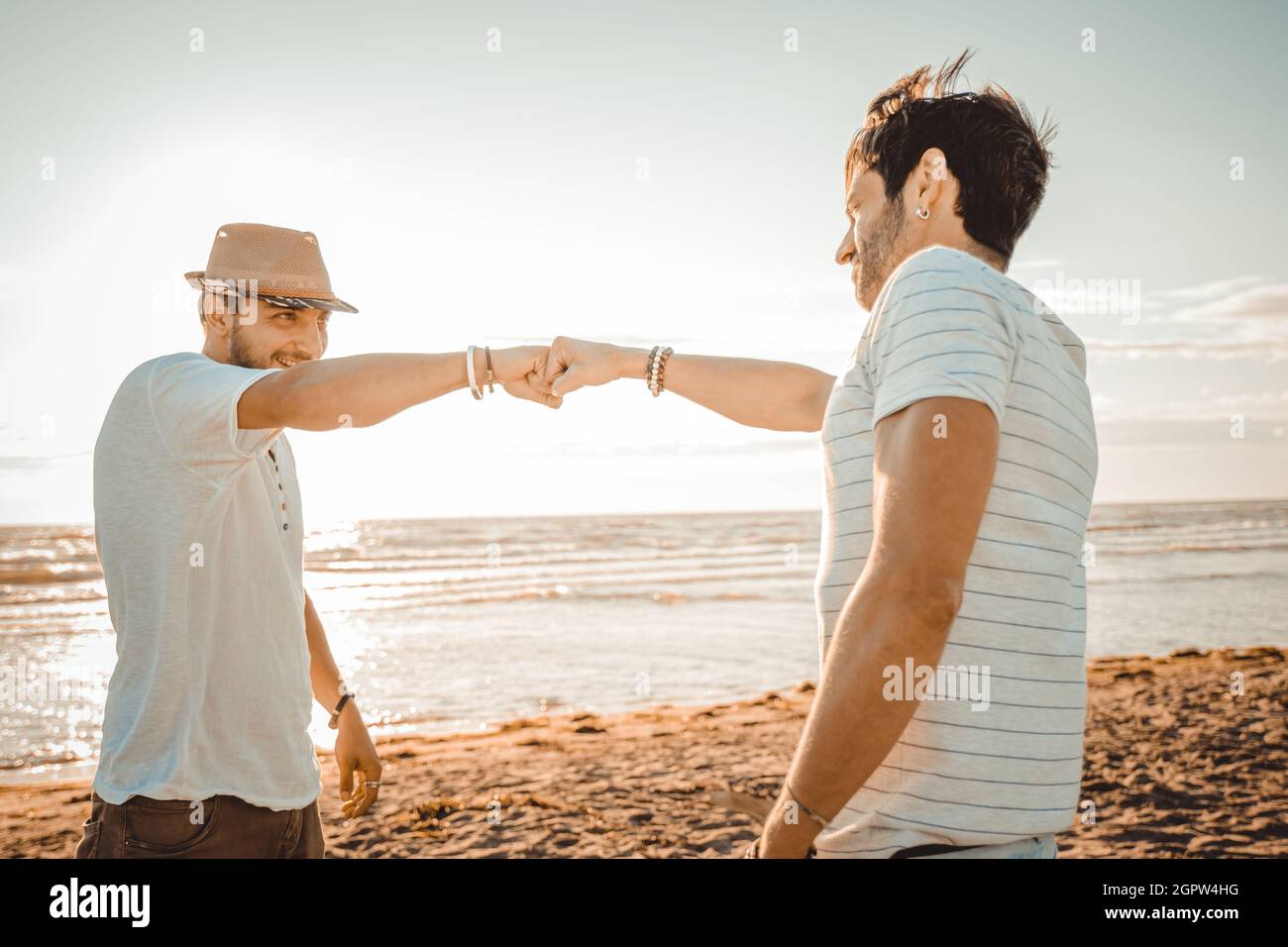 Two caucasian smiling guys on the beach greeting each other with touch ...