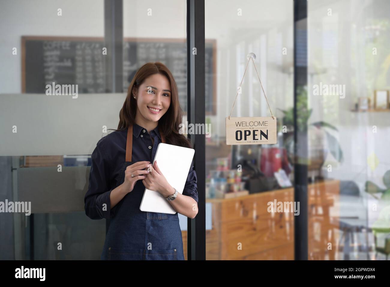Smiling female waitress holding digital tablet and standing in modern ...