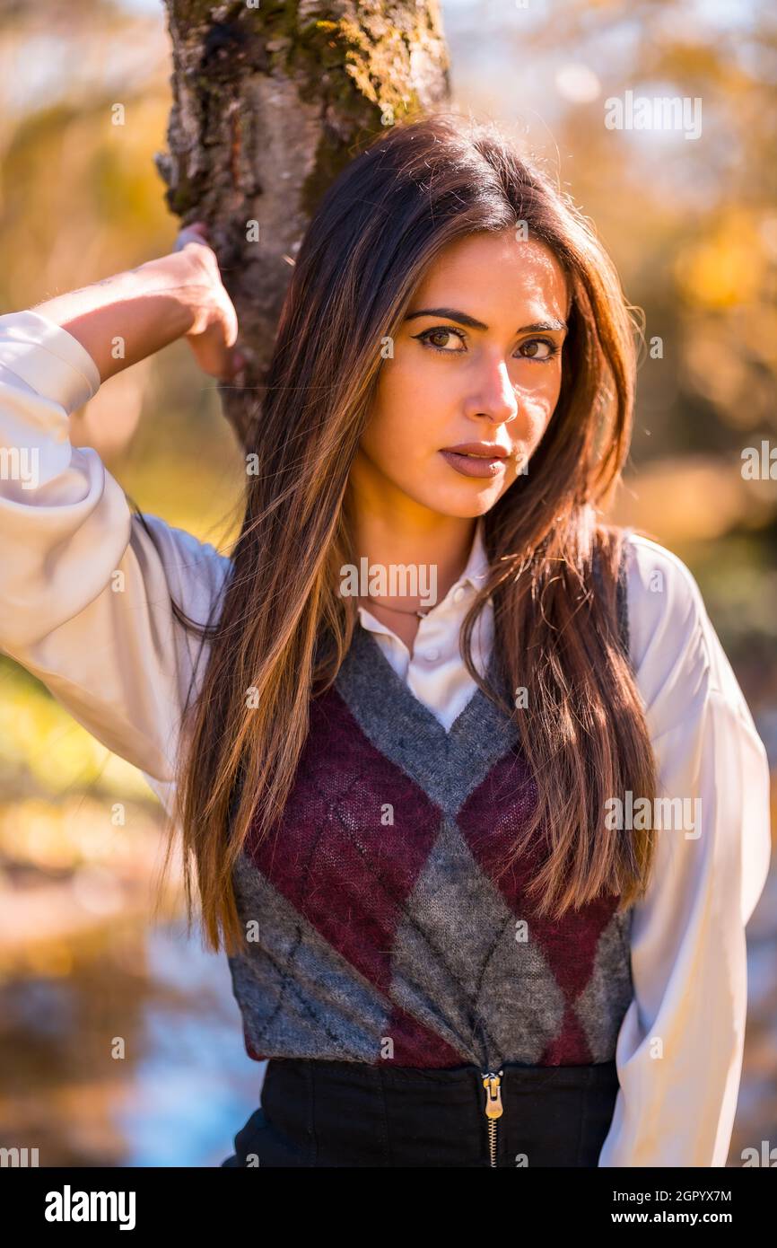A young Caucasian brunette college girl in a park next to a tree with a ...