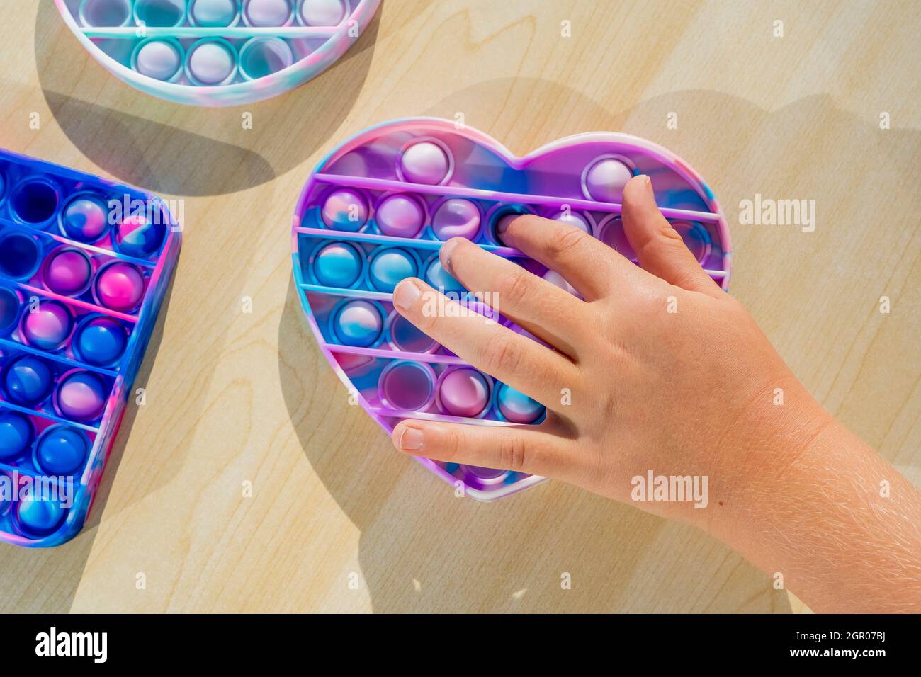 Little child playing with anti stress sensory pop it at wooden table ...
