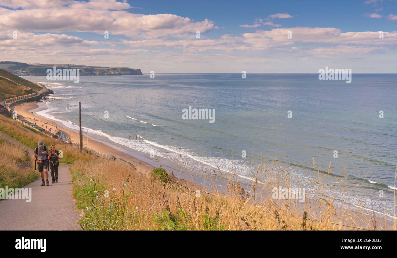 A panorama of cliffs and a headland. Paths lead down to a beach where a ...