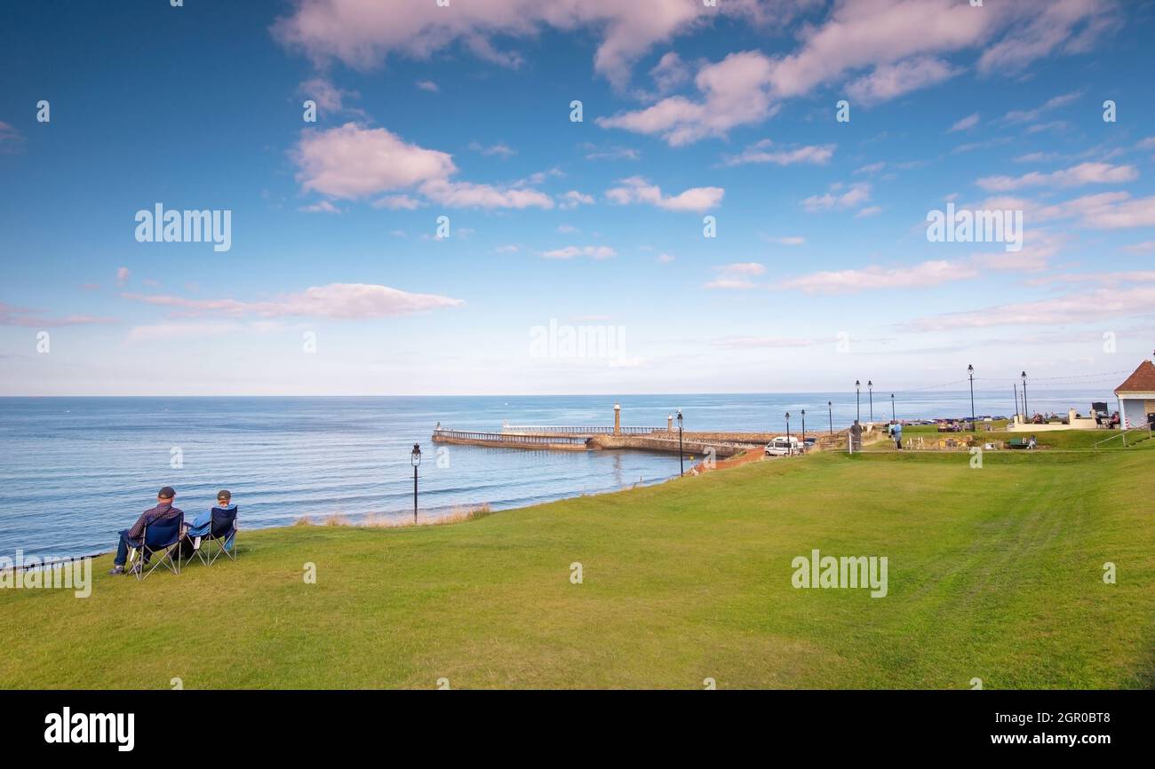 A cliff top overlooking the sea. A pier with a lighthouse stretches out ...