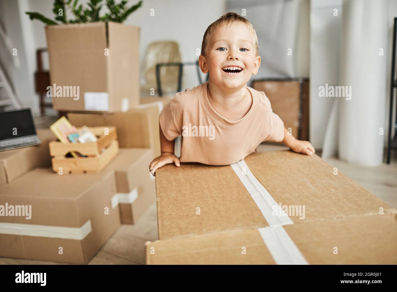 Portrait of cute happy boy moving boxes and playing while family ...