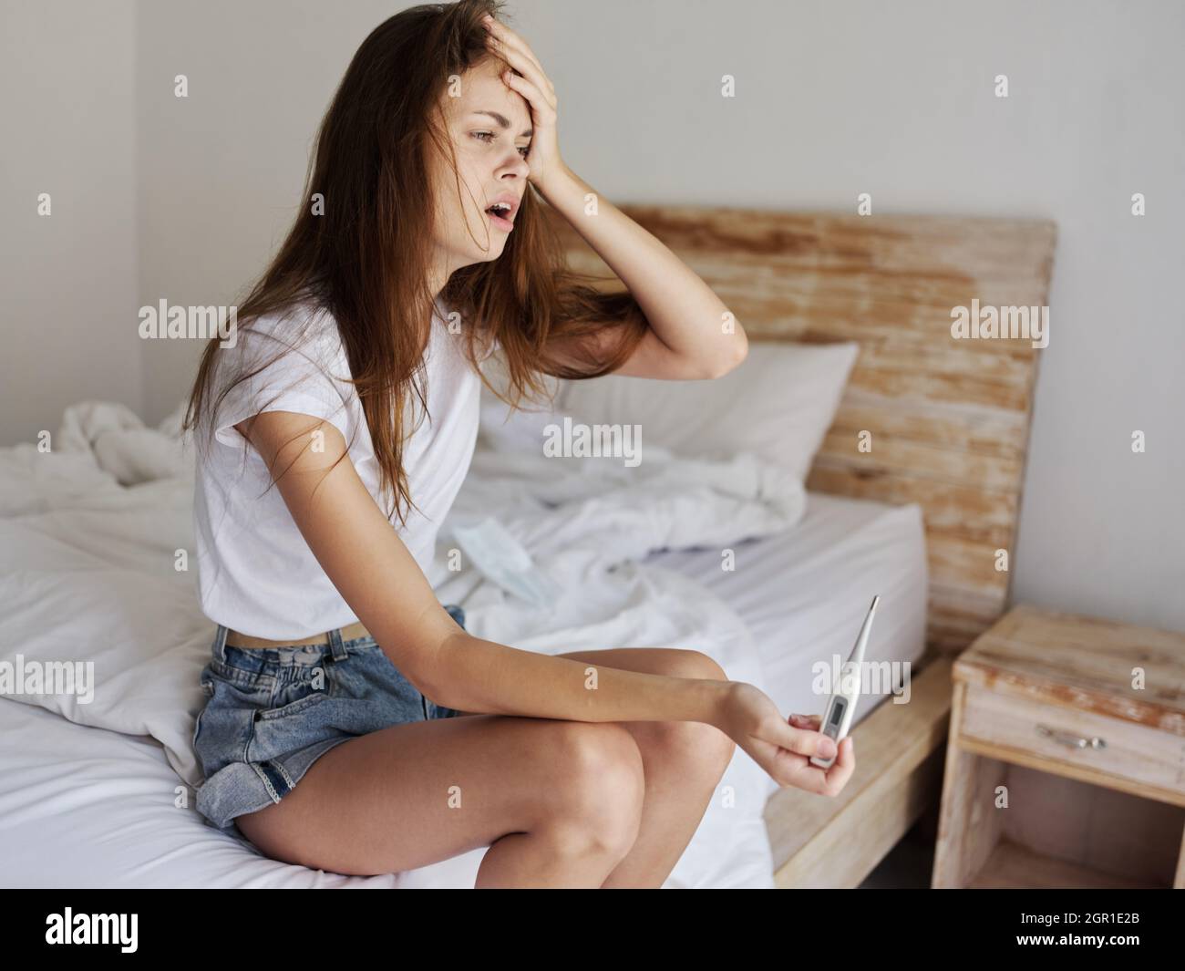 woman sitting on bed with a thermometer in her hands high temperature ...
