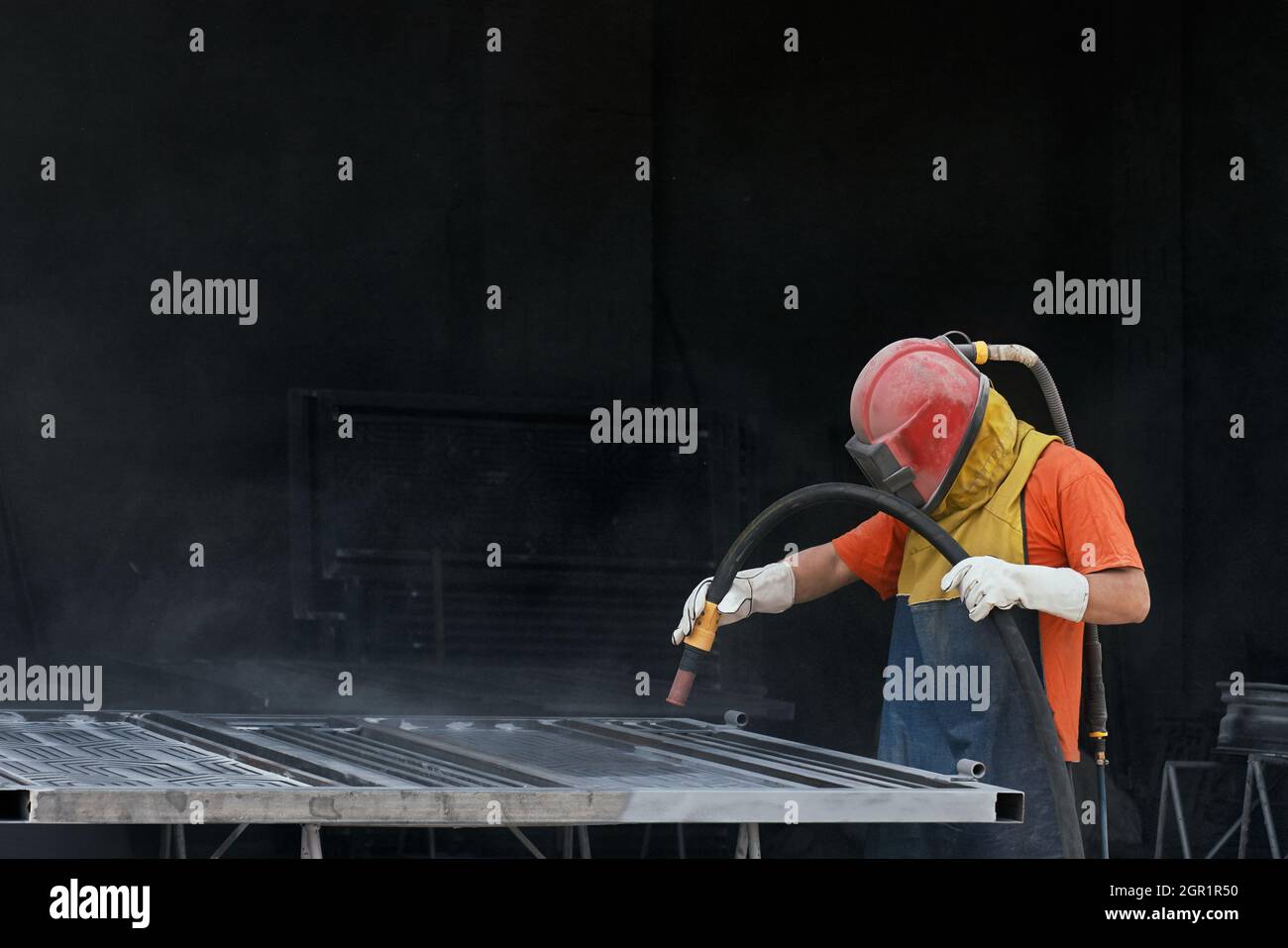 Industrial worker dressed in protective helmet and clothes sandblasting ...