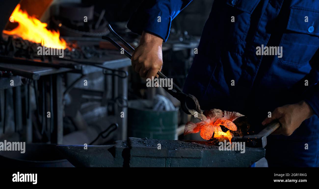 Man in blue uniform using hammer and pliers while working with molten ...