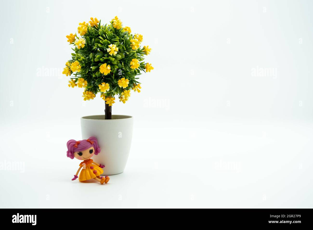 Close-up picture of a doll sitting near a toy tree isolated on a white ...