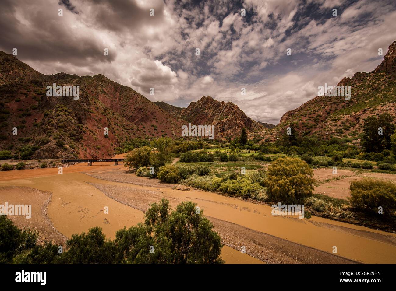 Red coloured river between dry mountains with a bridge and expressive ...