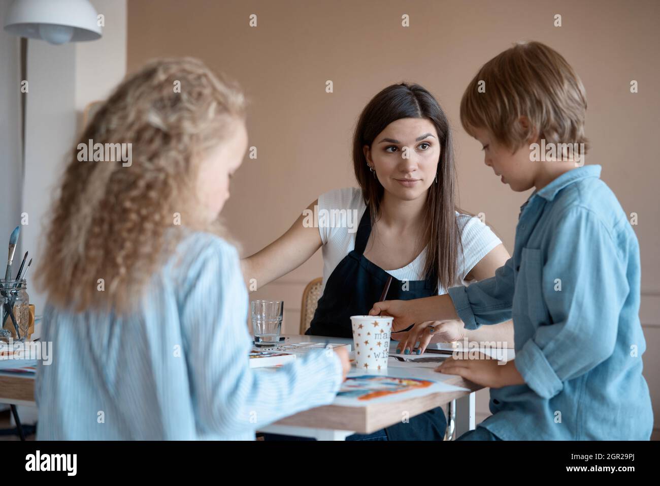 Group of kids and their teacher leaning over table with watercolor ...