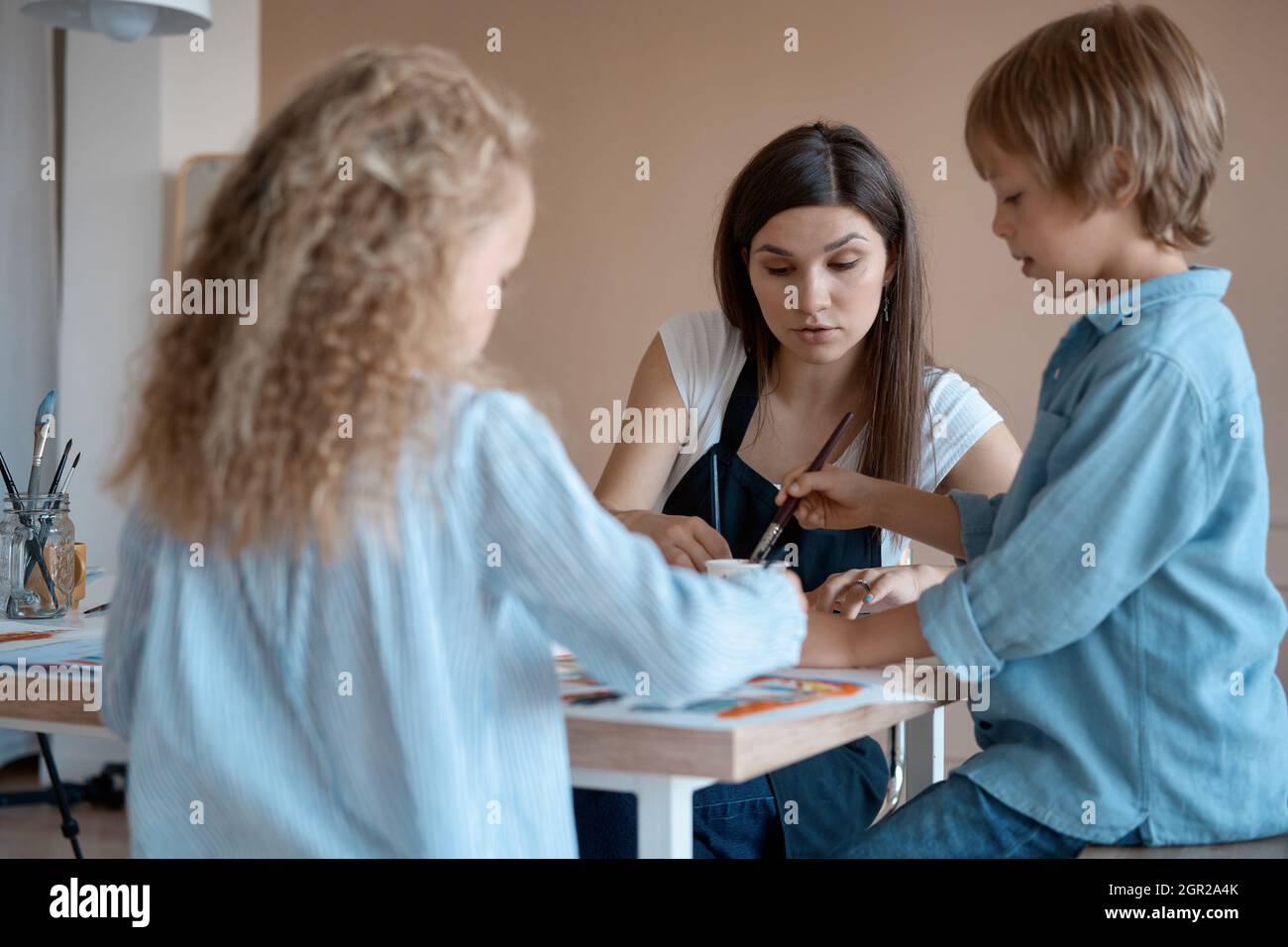 Group of kids and their teacher leaning over table with watercolor ...