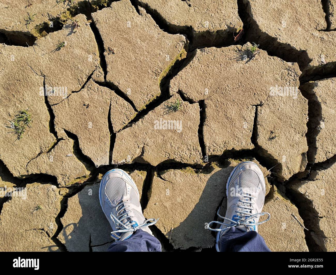 Top view of feet on the ground cracked by drought under the sunlight ...