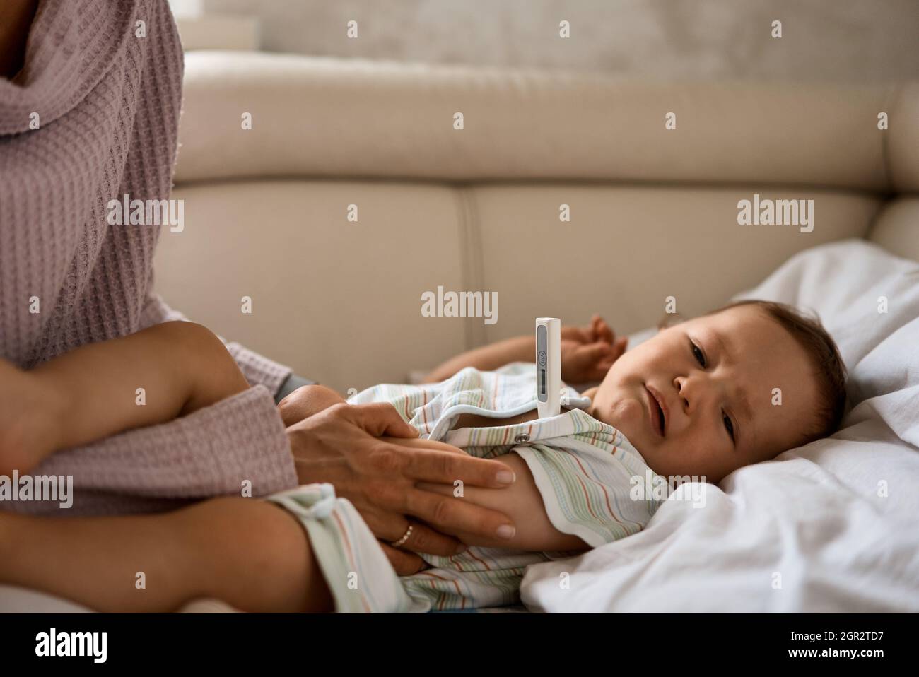 Mother measuring temperature of her ill kid at background. Sick child with high fever lying at ...