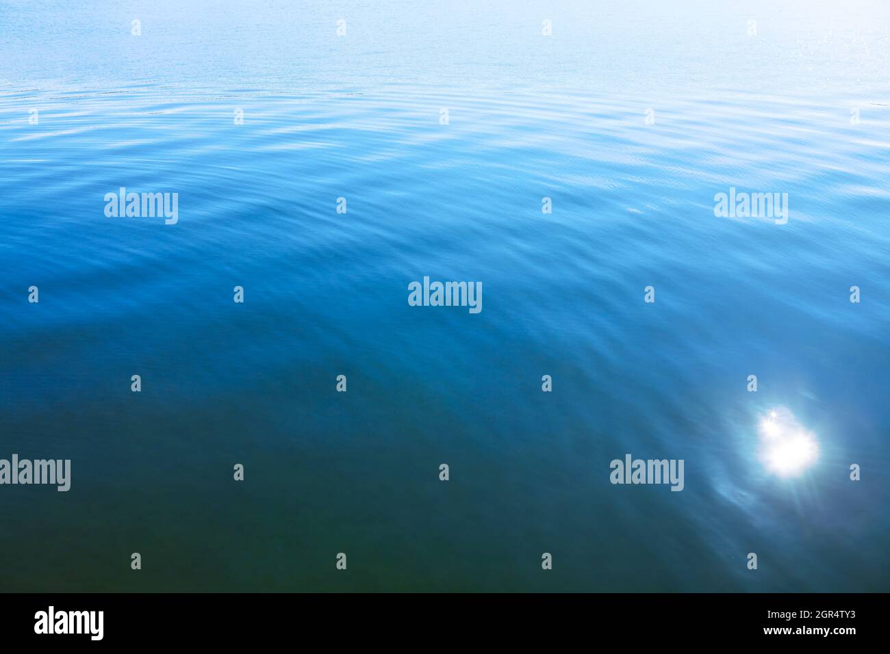Blue water surface with sun glowing reflection Stock Photo - Alamy