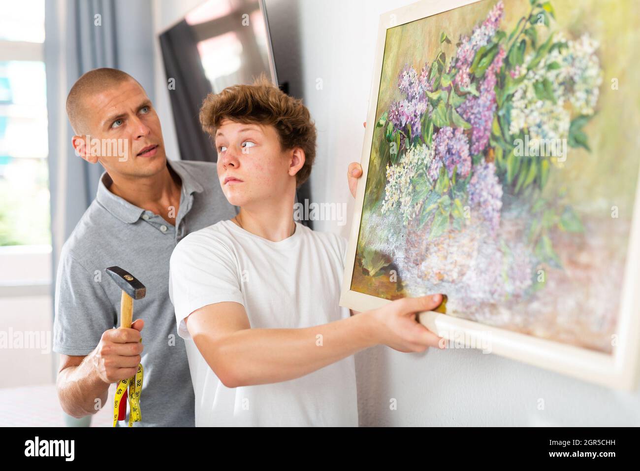Father shows his son how to hang painting on the wall of house Stock ...