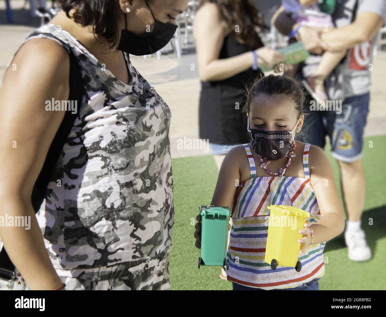 Caucasian girl with mask showing a woman the green and yellow garbage ...