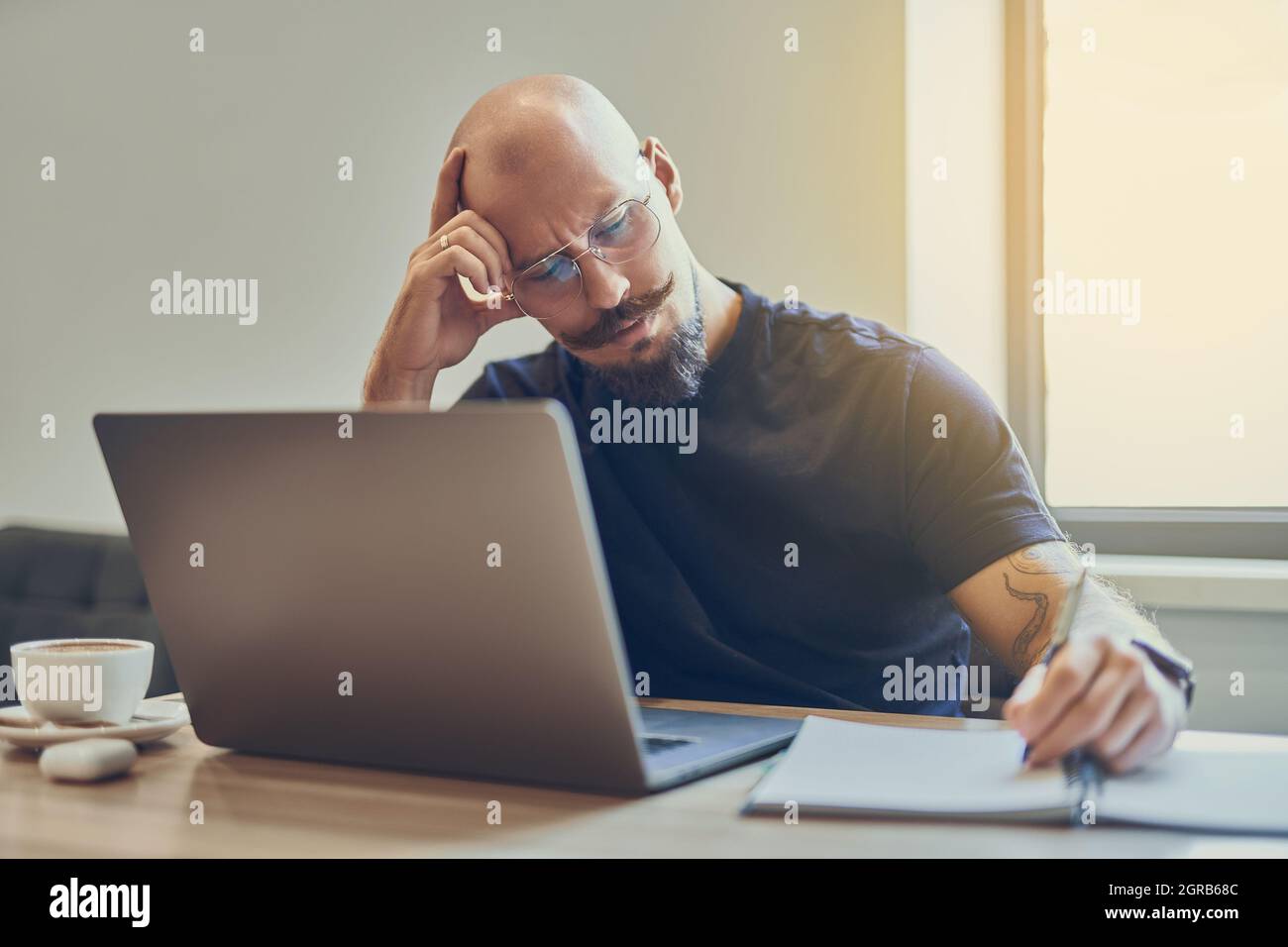 Adult caucasian bald man manager using laptop while writing notes in ...