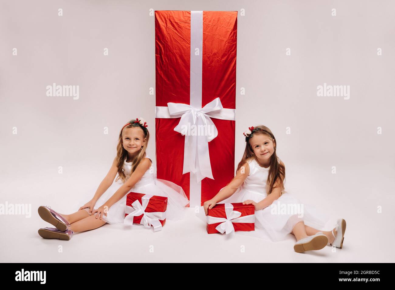 two little girls sit with Christmas gifts on a white background and a ...