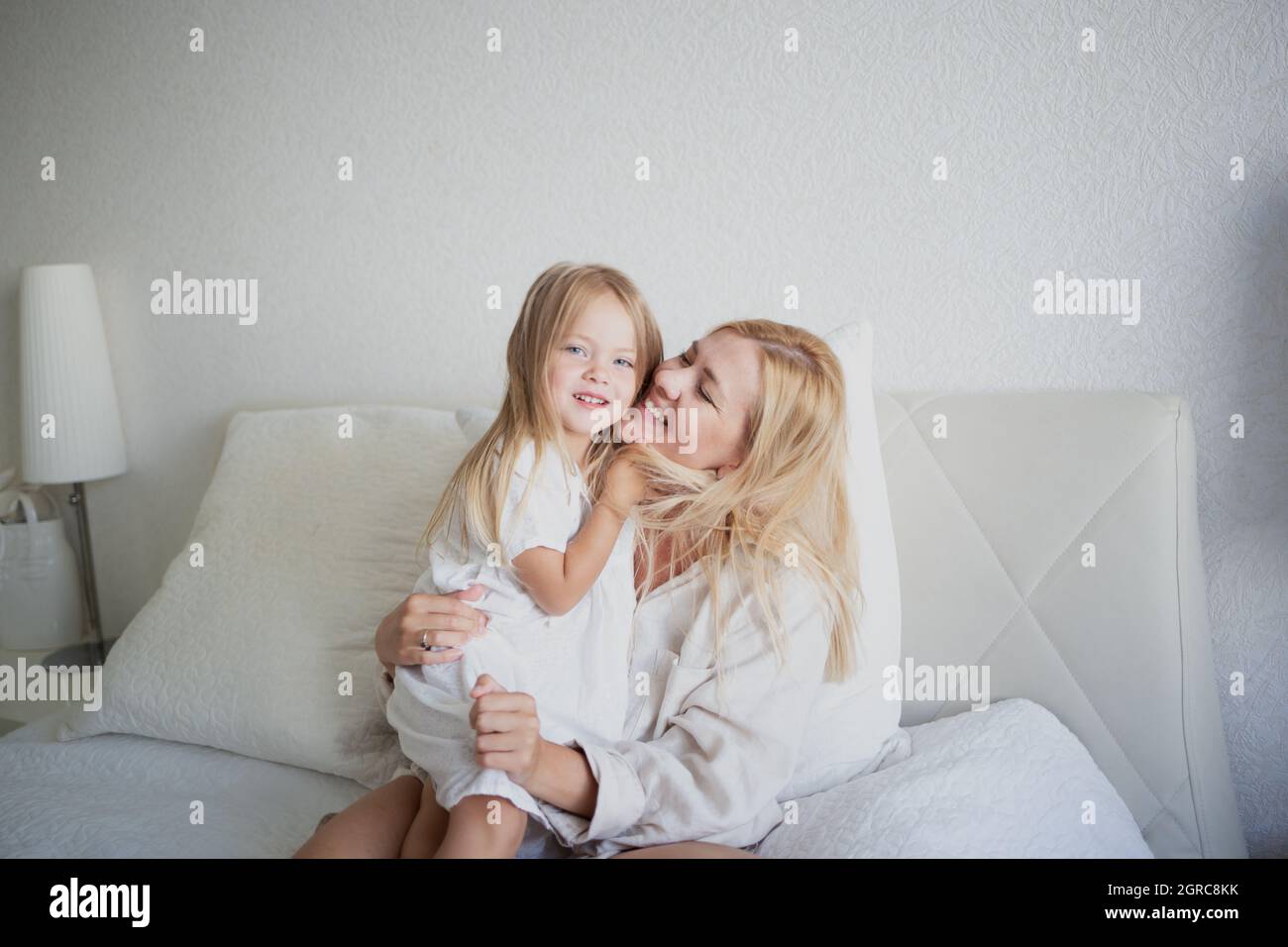 little girl hugging with mom while sitting on the bed in the bedroom ...