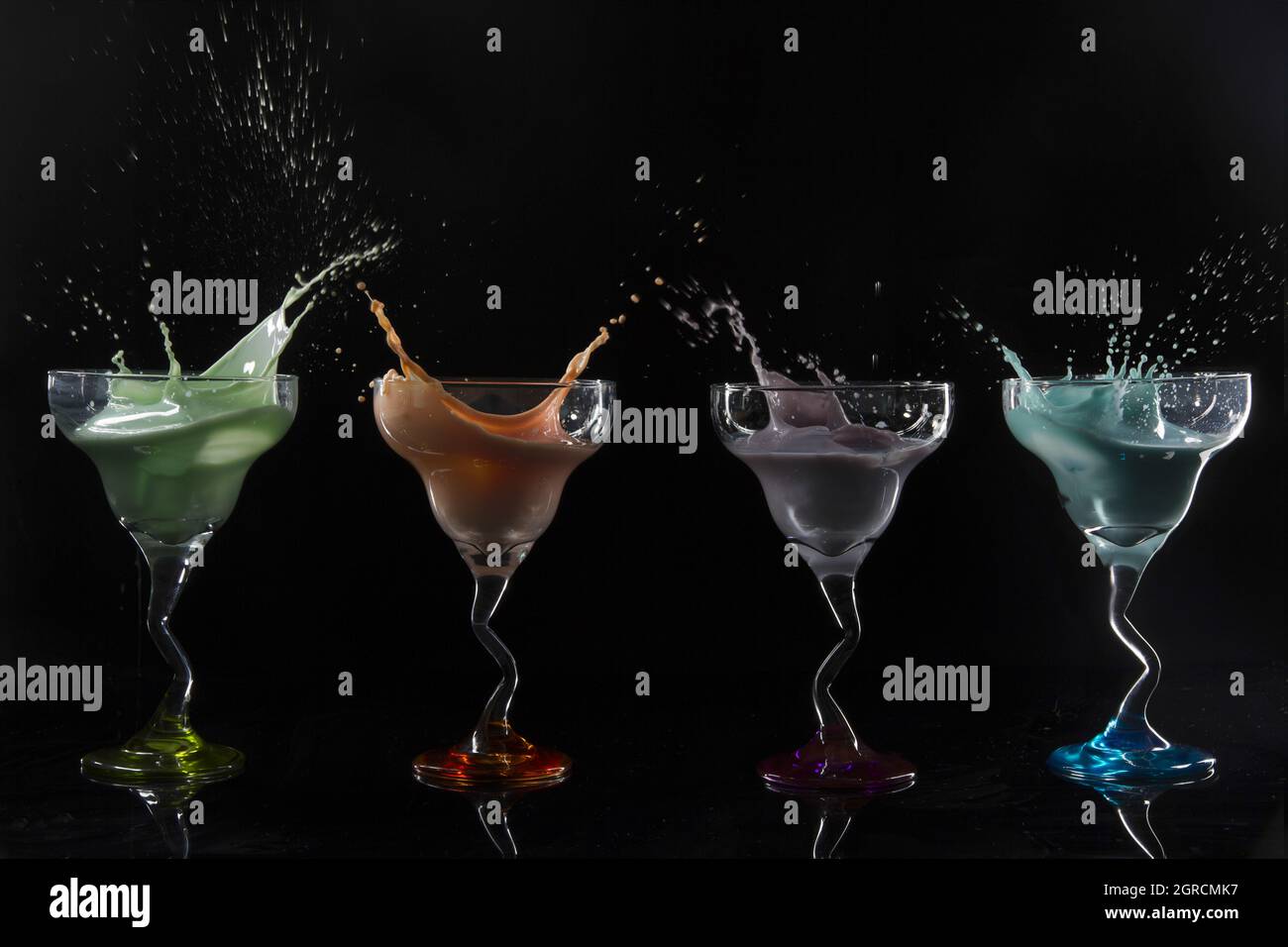 Cocktail glasses with colorful alcoholic drinks splashing on a black ...