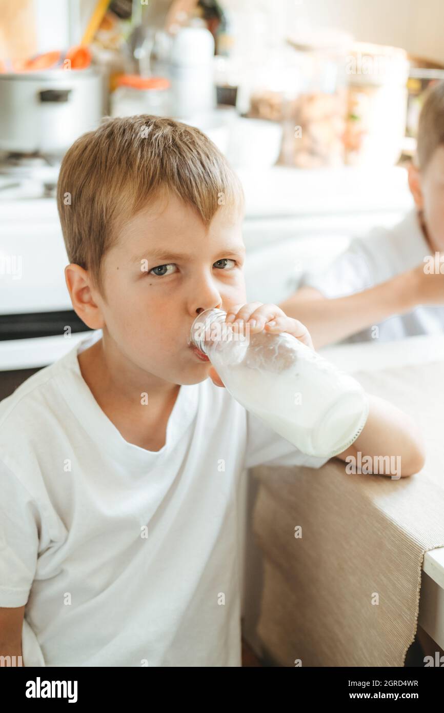A boy is drinking milk from a bottle in the kitchen at home. Morning ...