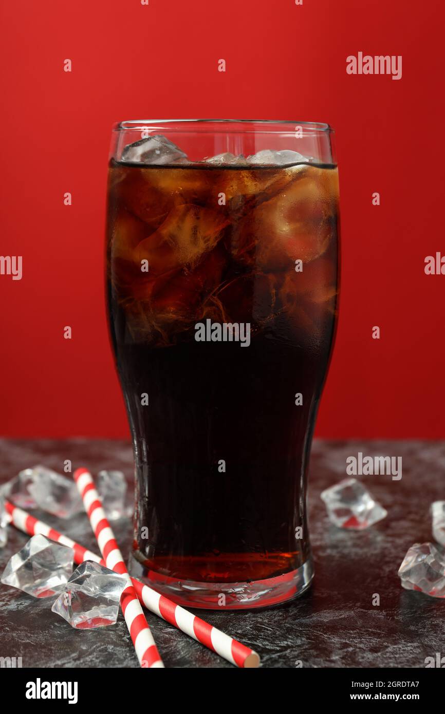 Glass of cola, ice and straws against red background Stock Photo - Alamy