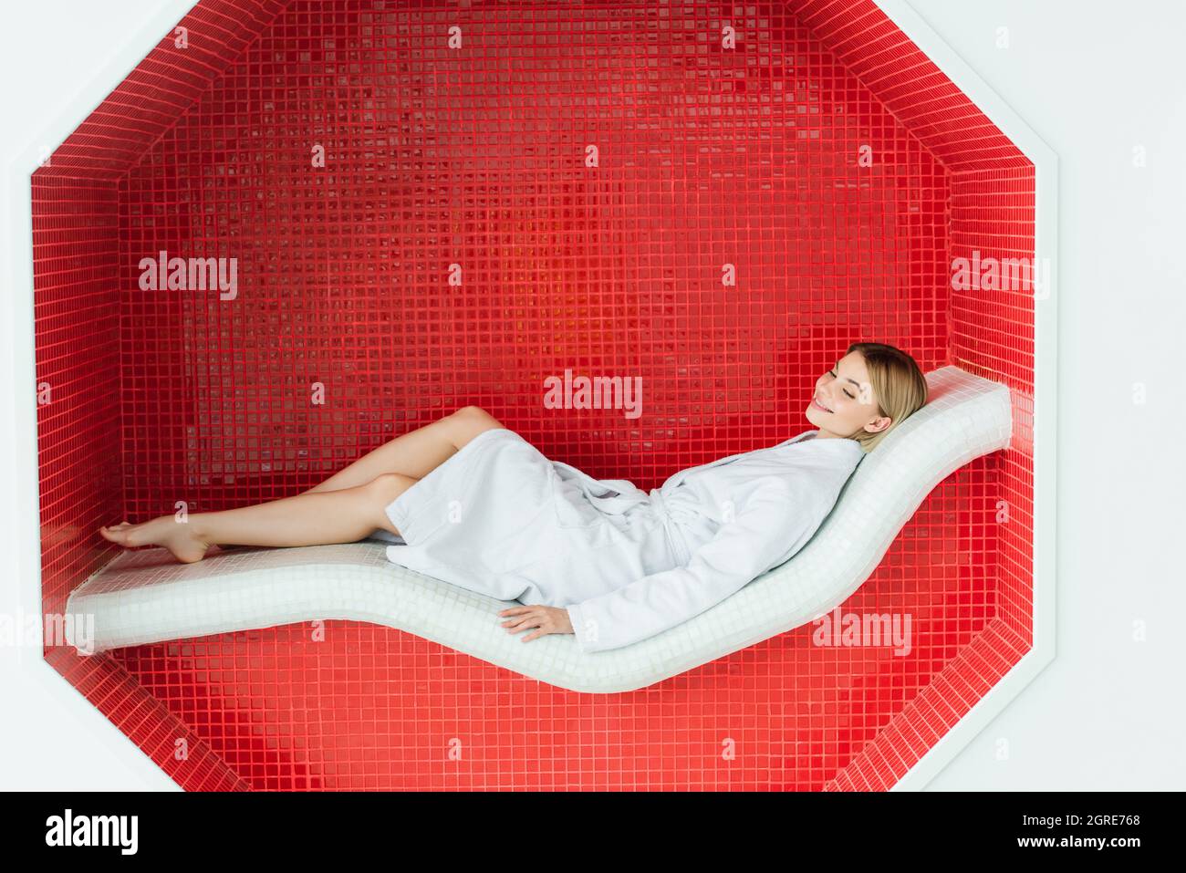 Cheerful woman in white bathrobe lying on lounge chair in spa center ...