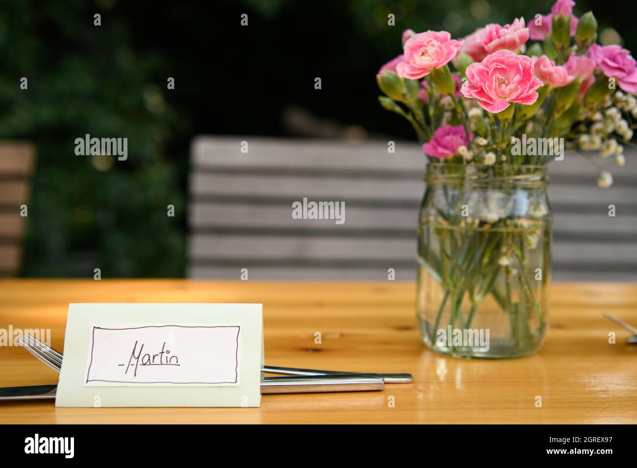 Hand written table name card and cutlery on a wooden table, flowers in ...
