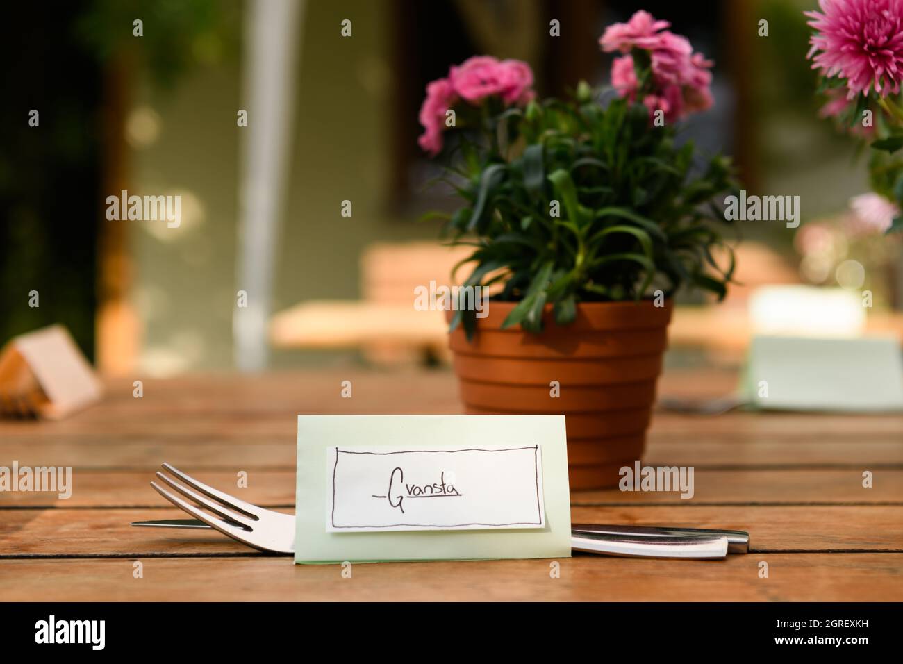 Hand written table name card and cutlery on a wooden table, flowers in ...